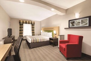 Quarto de hotel com cama, escrivaninha, cadeira, televisão e quadro na parede.