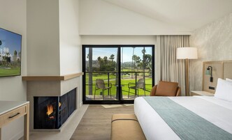 Quarto de hotel com cama grande, lareira, televisão e varanda com vista para um campo de golfe.