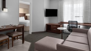 Quarto de hotel moderno com cama, escrivaninha, sofá, TV e janela com cortinas.