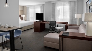 Quarto de hotel com cama, escrivaninha, cadeira de escritório, sofá e mesa de jantar com cadeiras.