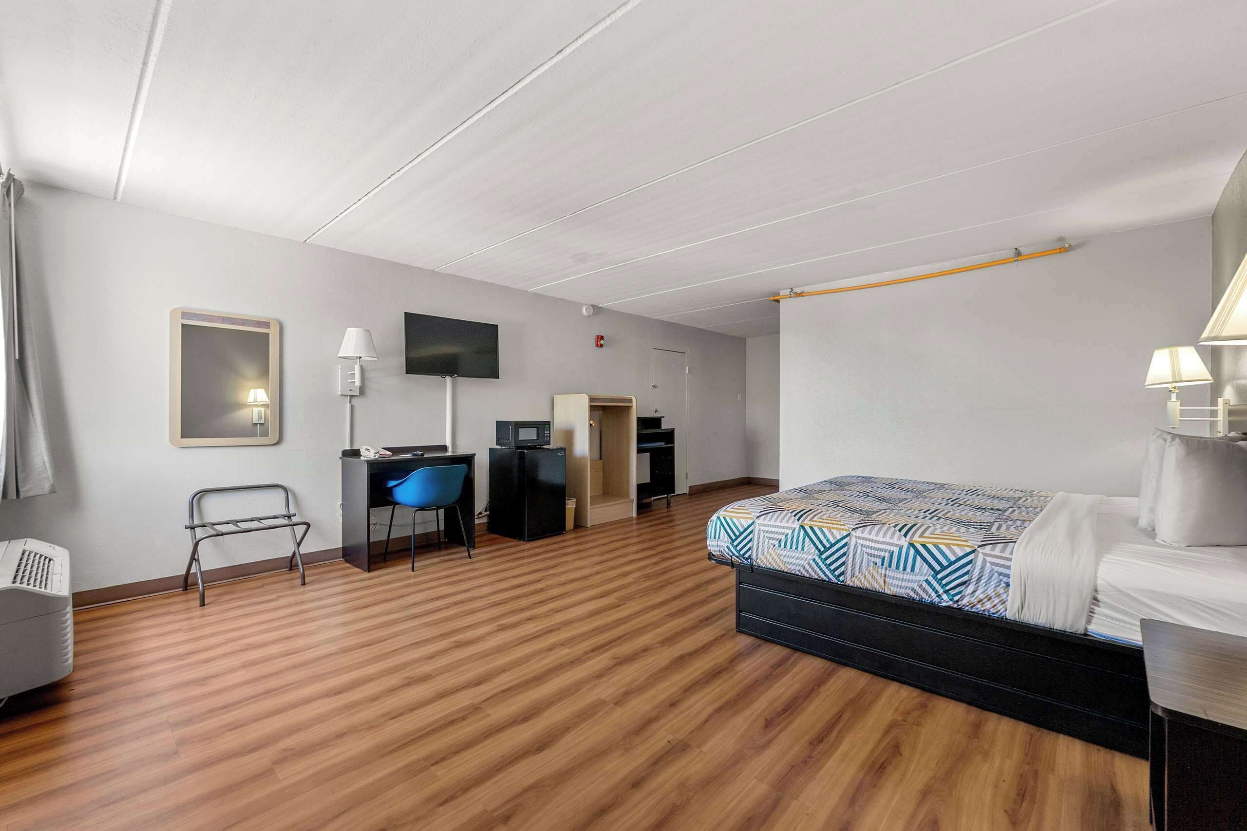 Quarto de hotel com cama, escrivaninha, cadeira e televisão na parede.