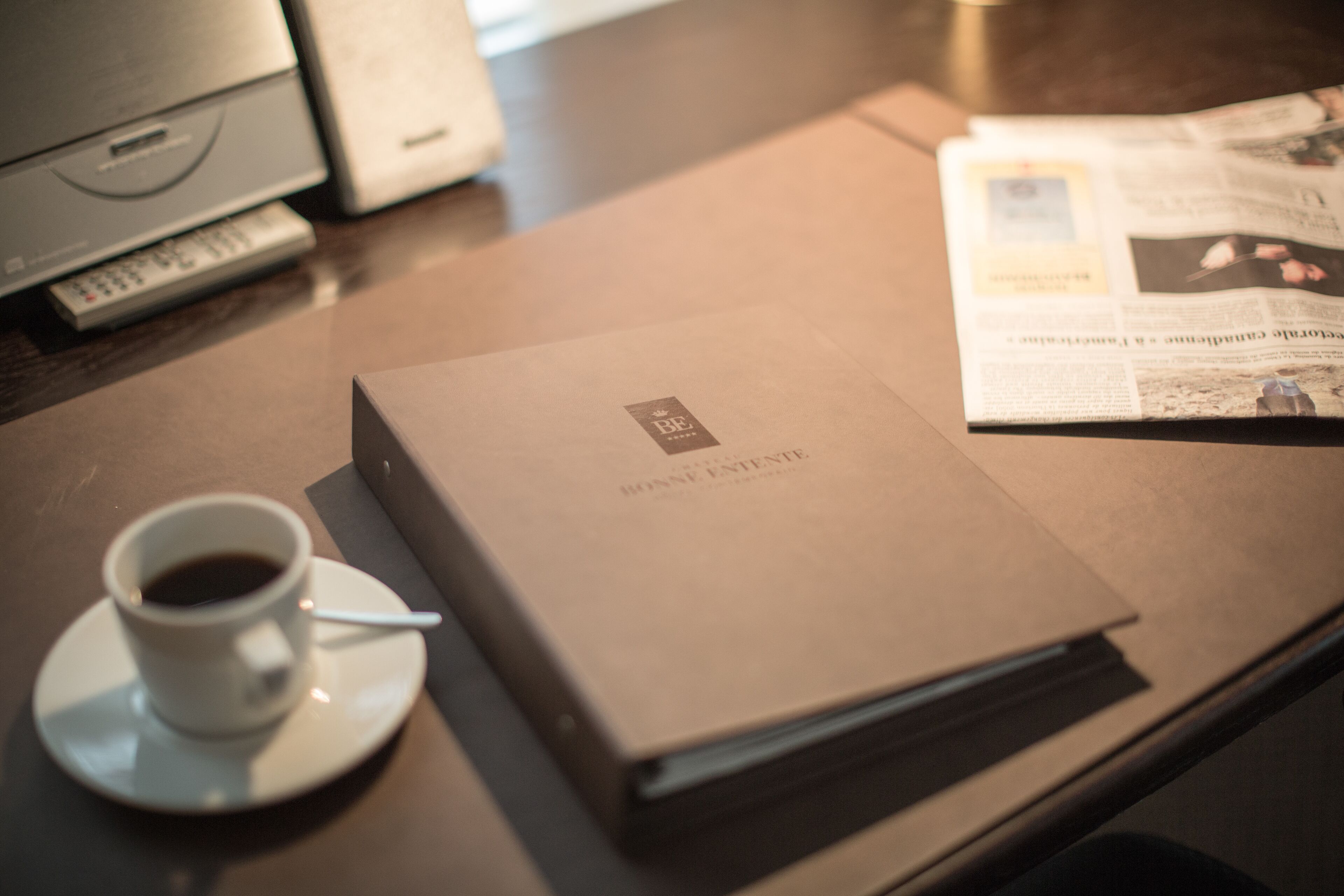 Uma mesa com uma xícara de café, um livro e um jornal.