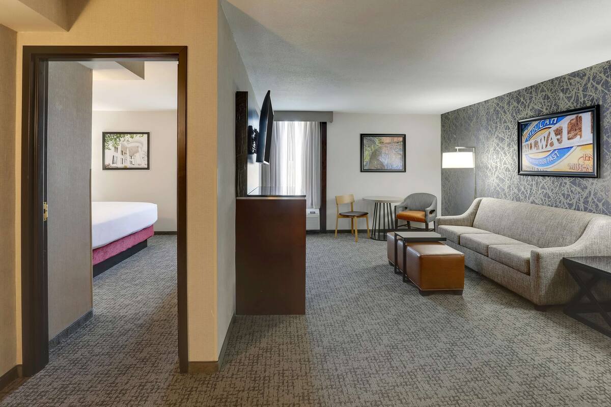 Quarto de hotel com cama, escrivaninha, sofá e televisão.