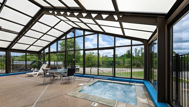 Piscina exterior coberta com mesa e cadeiras, rodeada por paredes de vidro e guarda-corpo de metal.