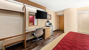 Quarto de hotel com escrivaninha, cadeira, televisão, micro-ondas e tapete vermelho.
