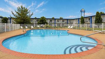 Piscina com borda de tijolos, cercada por uma cerca branca, e um letreiro Days Inn ao fundo.