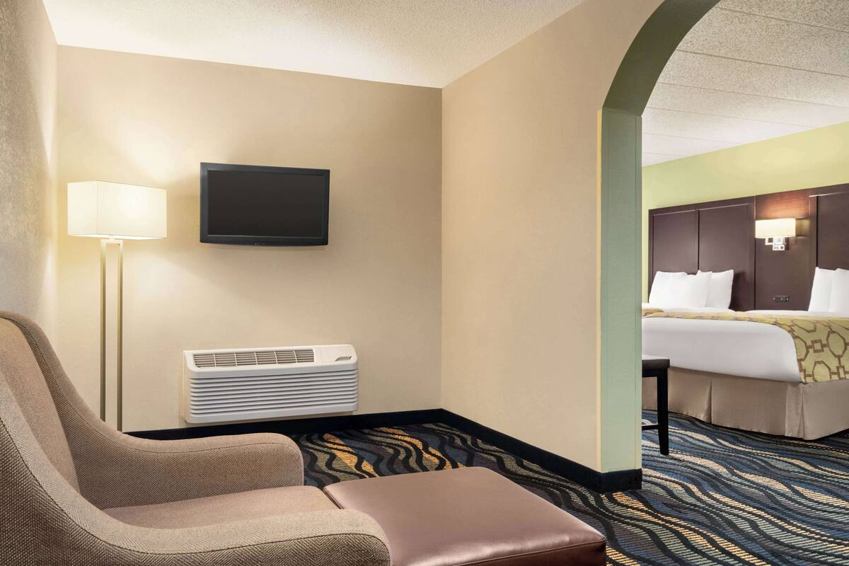 Quarto de hotel com uma cama, televisão fixada na parede, luminária e unidade de ar condicionado.