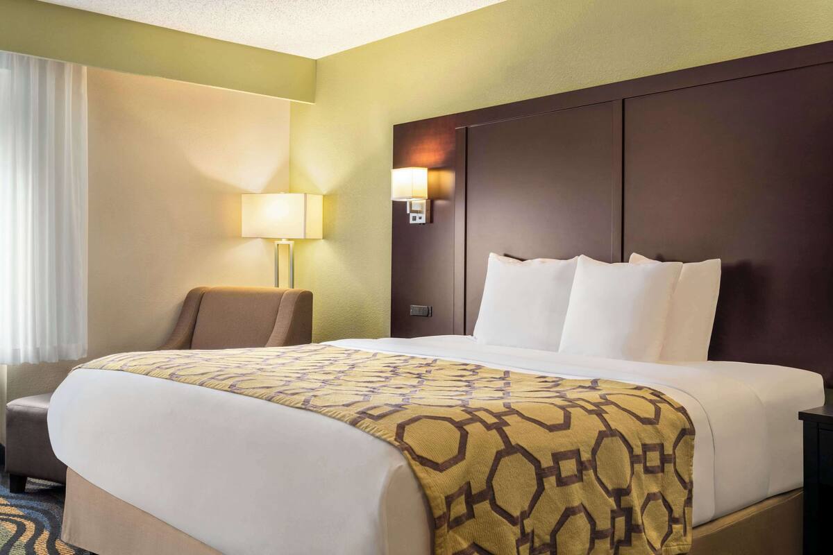 Quarto de hotel com uma cama grande, abajur, cadeira e luminária na parede.