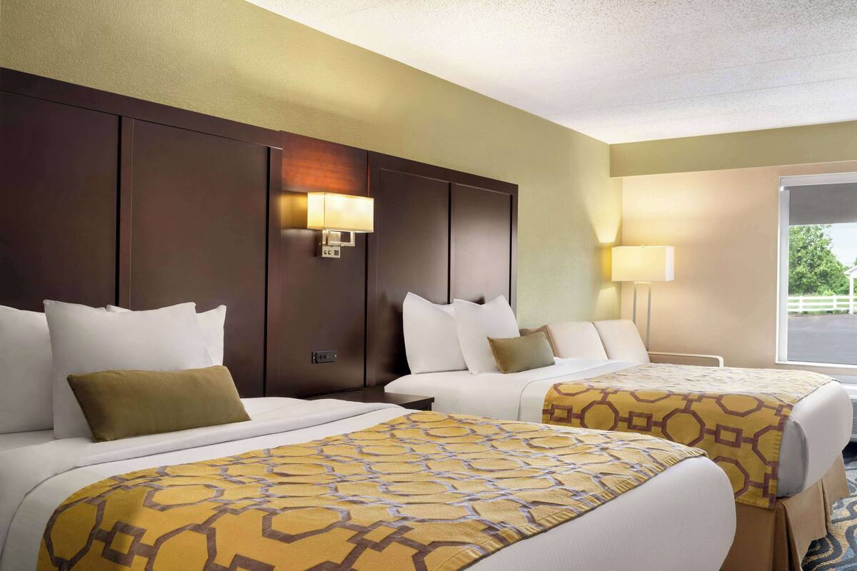 Quarto de hotel com duas camas, cada uma com colcha estampada, uma grande cabeceira de madeira escura e luminárias fixadas na parede.