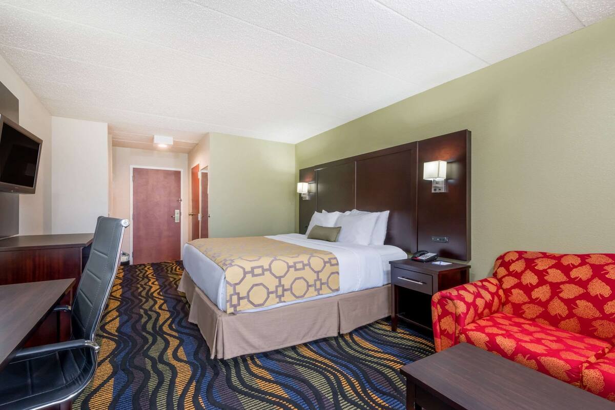 Quarto de hotel com cama, escrivaninha, cadeira, sofá e televisão.