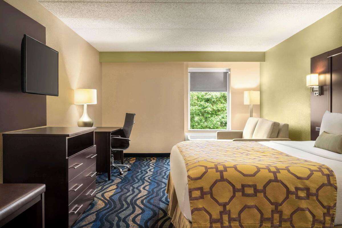 Quarto de hotel com uma cama, escrivaninha, cadeira e televisão fixada na parede.