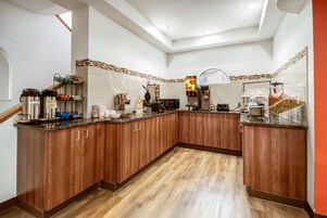 Cozinha moderna com armários de madeira, espaço para café, máquina de waffles e dispensador de suco.