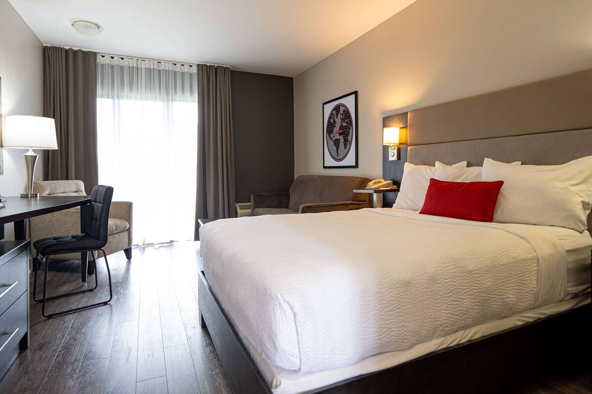 Quarto de hotel com uma cama grande, uma mesa com cadeira, um telefone e um quadro na parede.