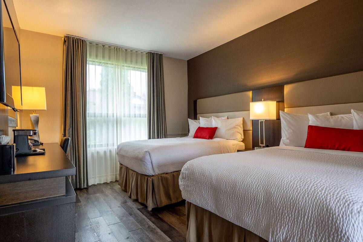Quarto de hotel com duas camas, uma escrivaninha e uma cadeira.
