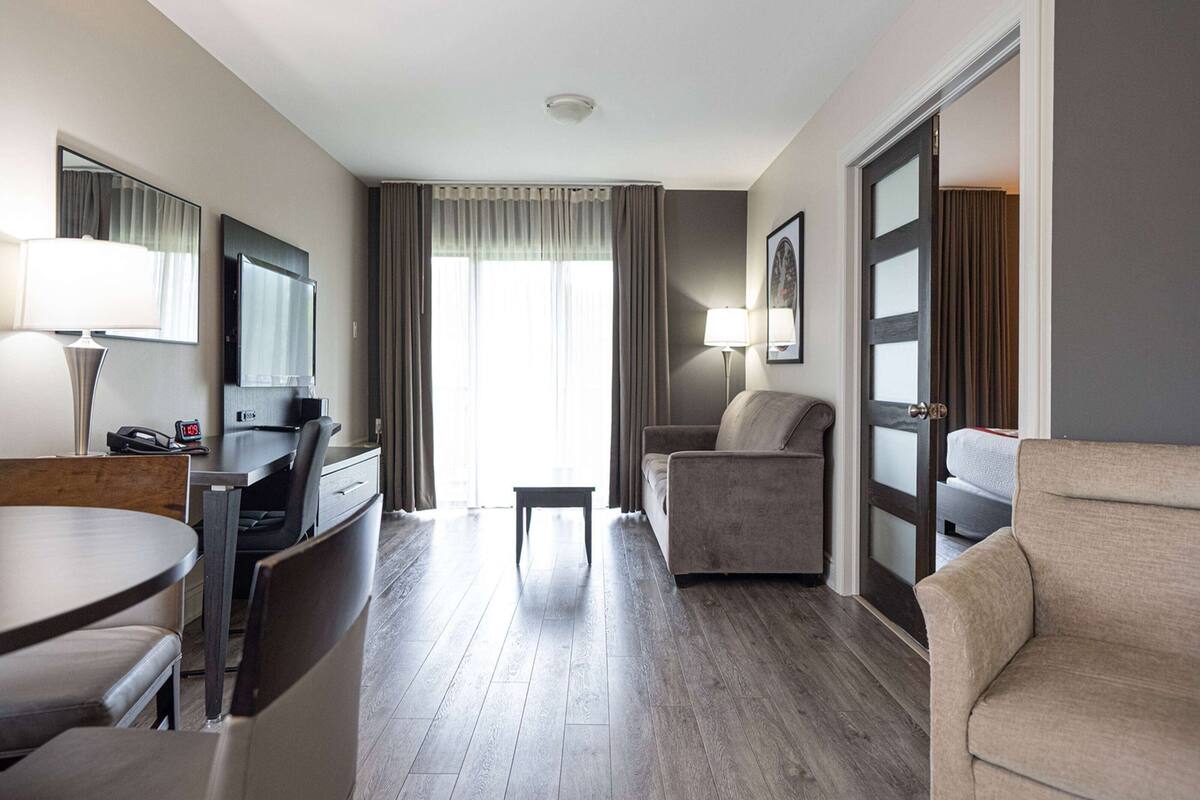 Quarto de hotel com área de refeições, sofá, televisão e porta que dá para outro espaço.