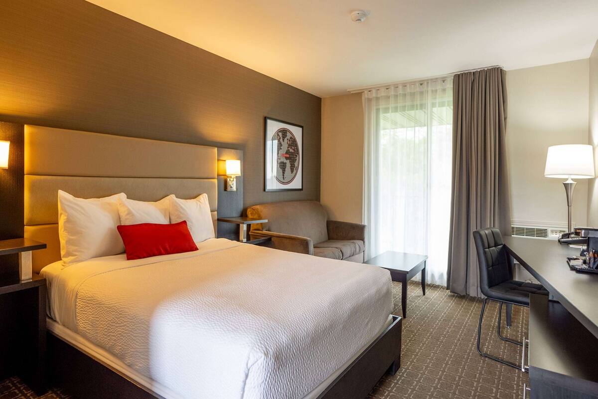 Quarto de hotel com uma cama grande, uma escrivaninha, uma cadeira e um sofá.