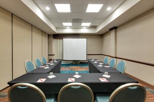 Uma sala de conferências com uma mesa comprida, cadeiras, uma tela de projetor e piso coberto de carpete.