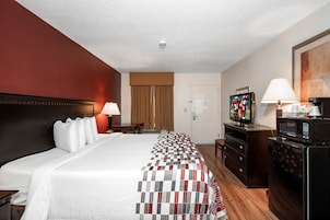 Quarto de hotel com cama, televisão, micro-ondas, cômoda, escrivaninha e porta.