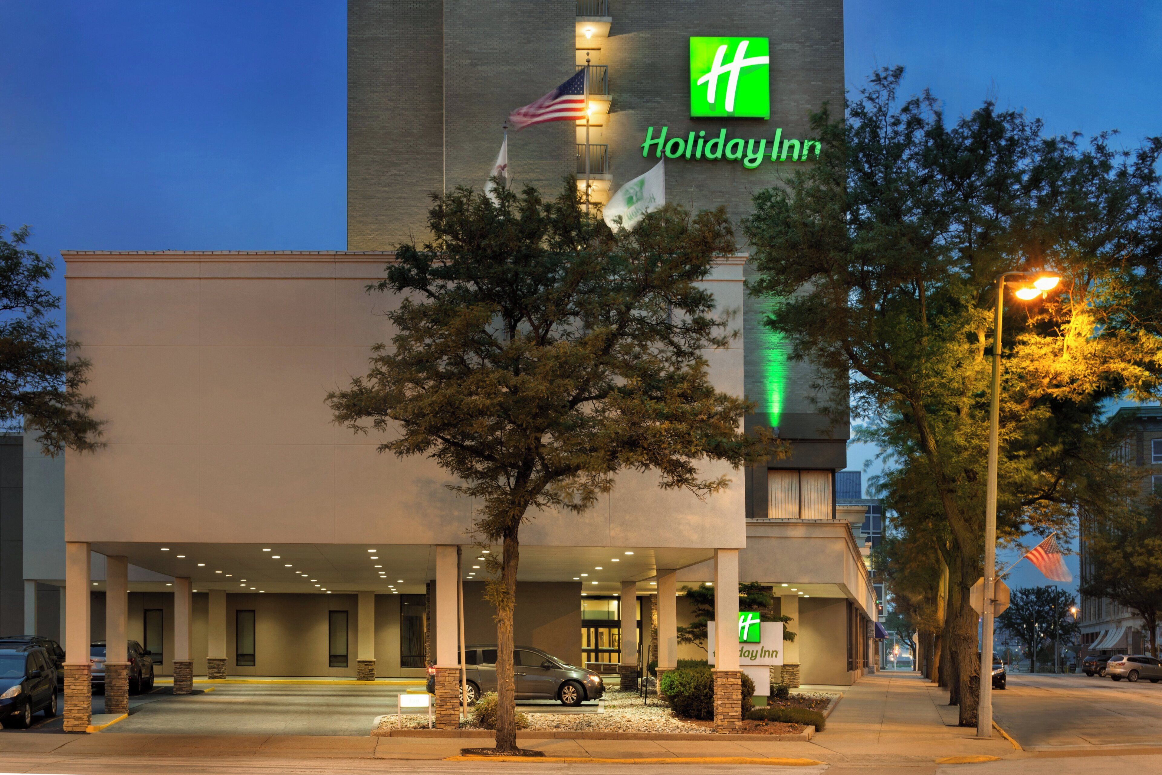 Um hotel Holiday Inn com fachada moderna, exibição da bandeira e área de estacionamento.