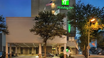 Um hotel Holiday Inn com fachada moderna, exibição da bandeira e área de estacionamento.