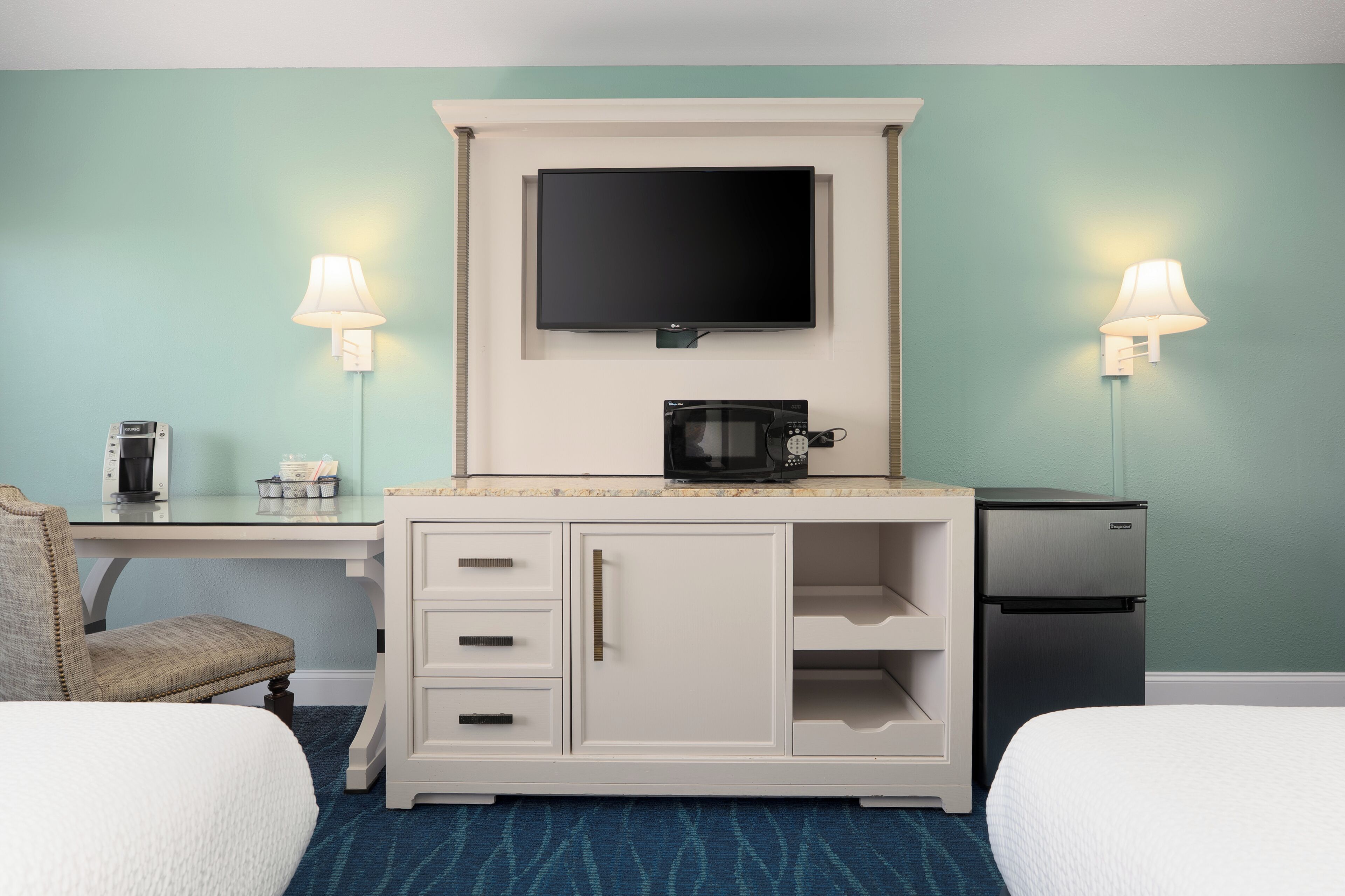 Quarto de hotel com duas camas, uma escrivaninha, televisão de tela plana, micro-ondas e geladeira.