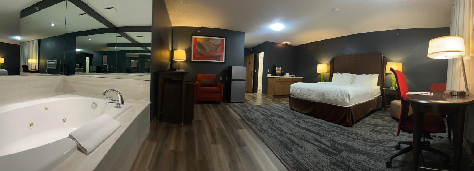Quarto de hotel com uma banheira grande, uma cama, uma escrivaninha e uma cadeira.