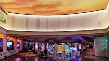 Um cassino com máquinas caça-níqueis, um bar e um teto com design inspirado no pôr do sol.