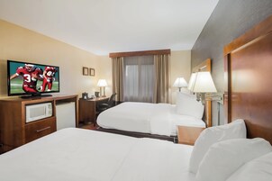 Quarto de hotel com uma cama, uma secretária com televisão, um micro-ondas e duas luminárias.
