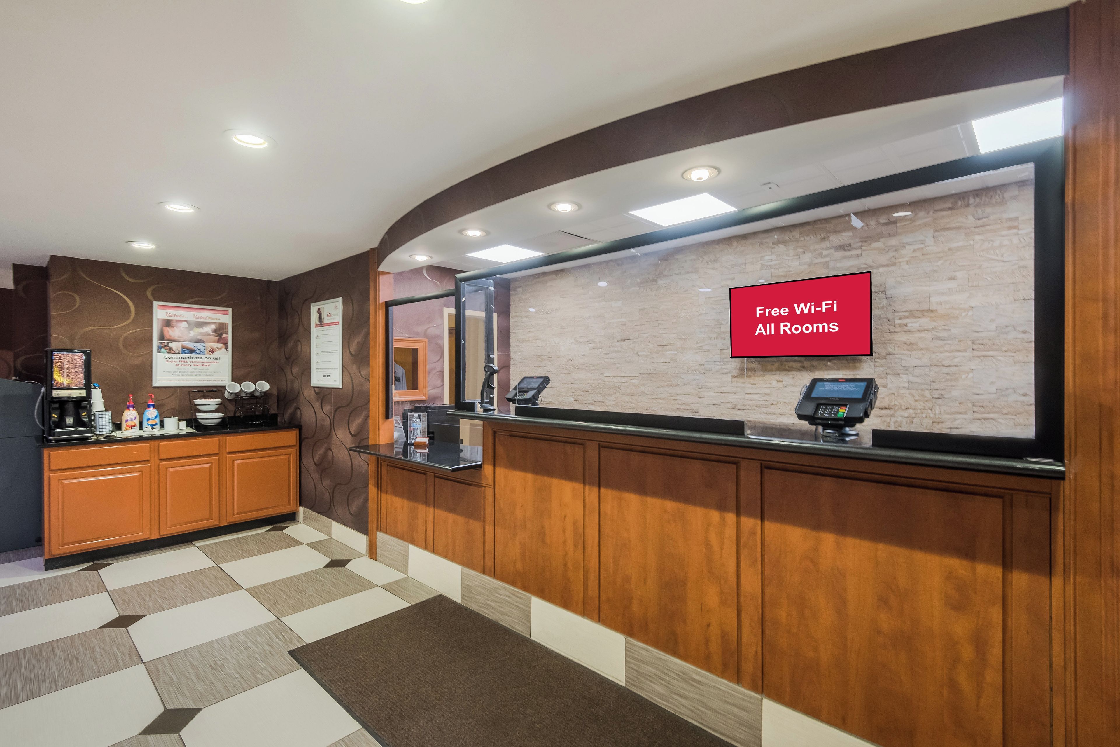 Uma área de recepção de hotel com balcão de check-in, máquina de café e placa indicando Wi-Fi gratuito em todos os quartos.