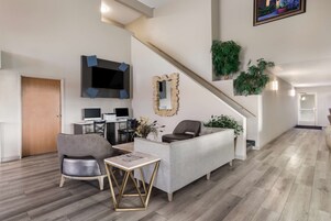 Uma sala de estar moderna com sofá, cadeiras, uma mesa pequena, televisão e escada.