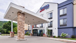 Um hotel Fairfield Inn & Suites com entrada coberta, pilares de pedra e área ajardinada com flores.