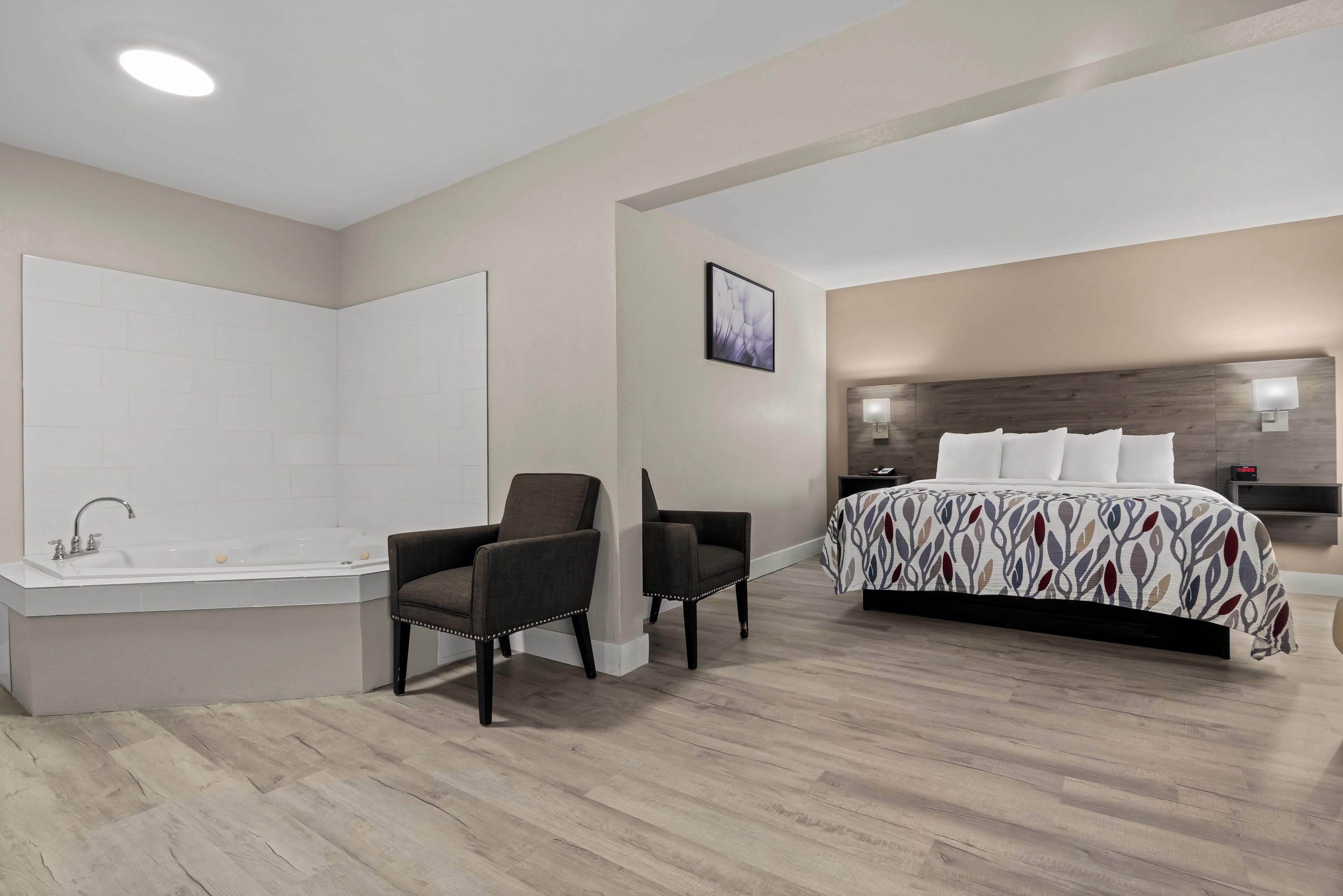 Quarto moderno com uma cama grande, área de estar com duas cadeiras, banheiro com banheira e uma luminária no teto.