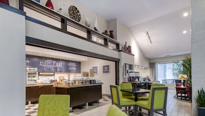 Um hall de hotel moderno com um bar de café, área de estar e uma escadaria para um andar superior.