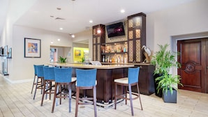 Uma área de bar moderna com uma televisão grande, banquetas e diversos tipos de garrafas.