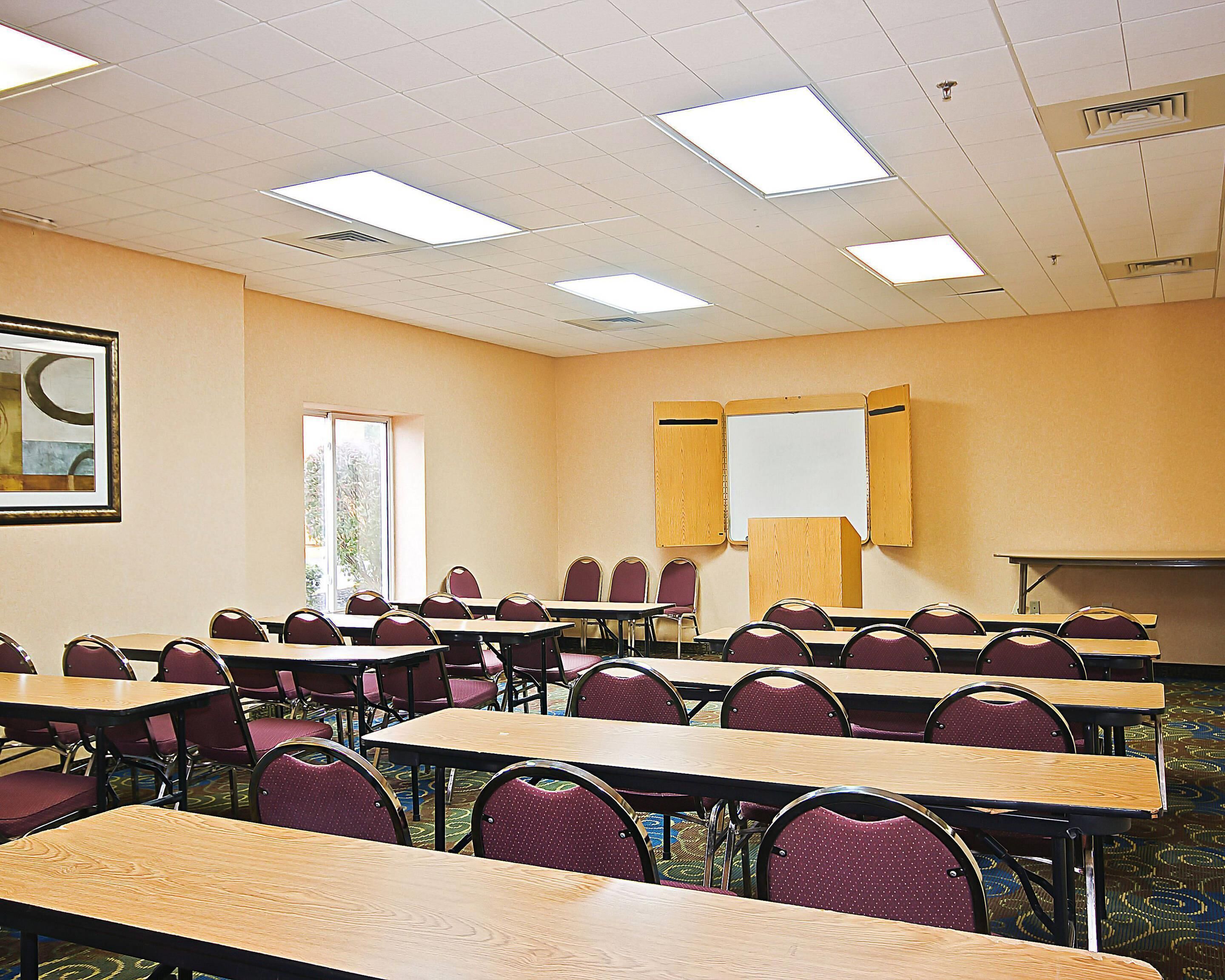 Uma sala de conferências com mesas, cadeiras, um quadro branco e uma janela.