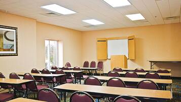 Uma sala de conferências com mesas, cadeiras, um quadro branco e uma janela.