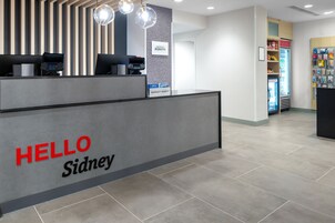 Uma receção com um letreiro 'HELLO Sidney', um posto de autoatendimento, um minibar e uma máquina de vendas automática.