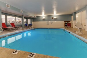 Piscina interna com água cristalina, indicadores de profundidade e cadeiras de descanso.
