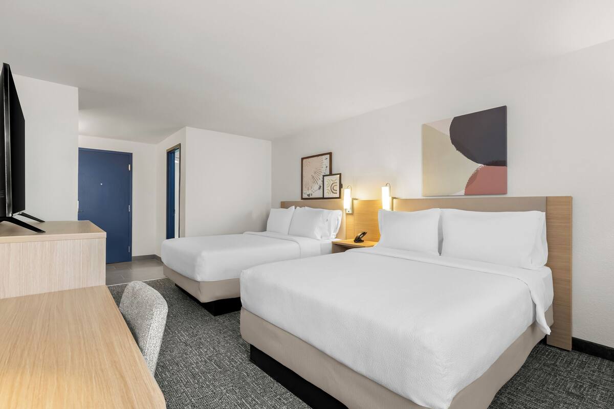 Quarto de hotel com duas camas, uma mesa e uma televisão.