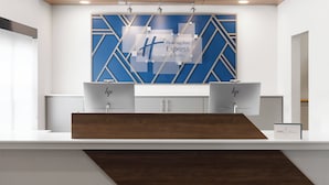 Um balcão de recepção com um design geométrico azul na parede, dois computadores HP e uma placa indicando Prêmios IHG.