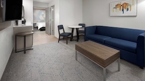 Uma sala de estar moderna com um sofá azul, uma mesa de centro de madeira e duas cadeiras. Há também uma pequena mesa redonda e uma televisão de tela plana fixada na parede.