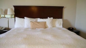 Cama bem arrumada com cabeceira de madeira, travesseiros brancos e almofada bege.