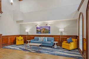 Um hall de entrada com um sofá azul, poltronas amarelas, uma mesa de centro e um quadro na parede.