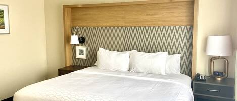 Quarto de hotel com uma cama grande, cabeceira de madeira, mesa de cabeceira com abajur e um quadro na parede.