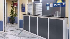 Uma área de recepção com piso de mármore, balcão de atendimento, uma planta e uma placa da Days Inn.