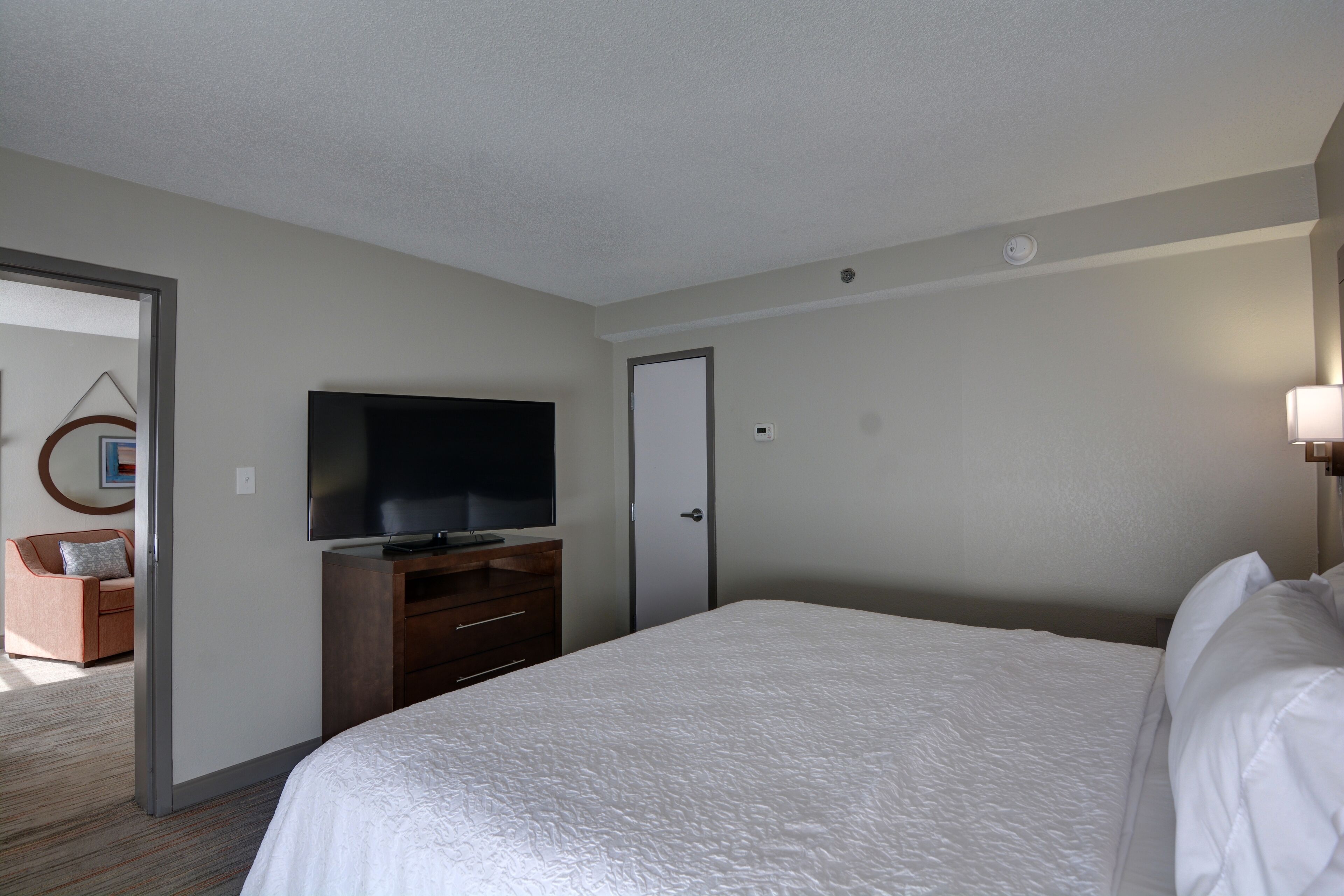 Quarto de hotel com uma cama grande, televisão de tela plana, cómoda de madeira e uma porta.