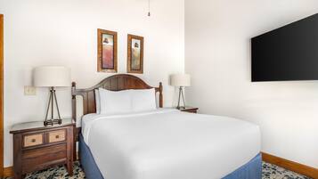 Quarto de hotel com cama grande, duas mesinhas de cabeceira, televisão de tela plana na parede e duas fotos emolduradas acima da cama.