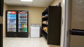 Quarto pequeno com duas geladeiras Coca-Cola, um mini-refrigerador e uma prateleira com lanches.