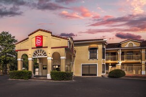 Um Red Roof Inn com arquitetura tradicional, destacando uma placa vermelha, janelas em arco e uma varanda no segundo andar.