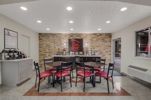 Cozinha moderna com painel de pedra, ilha central com máquina de café e área de jantar com cadeiras vermelhas.